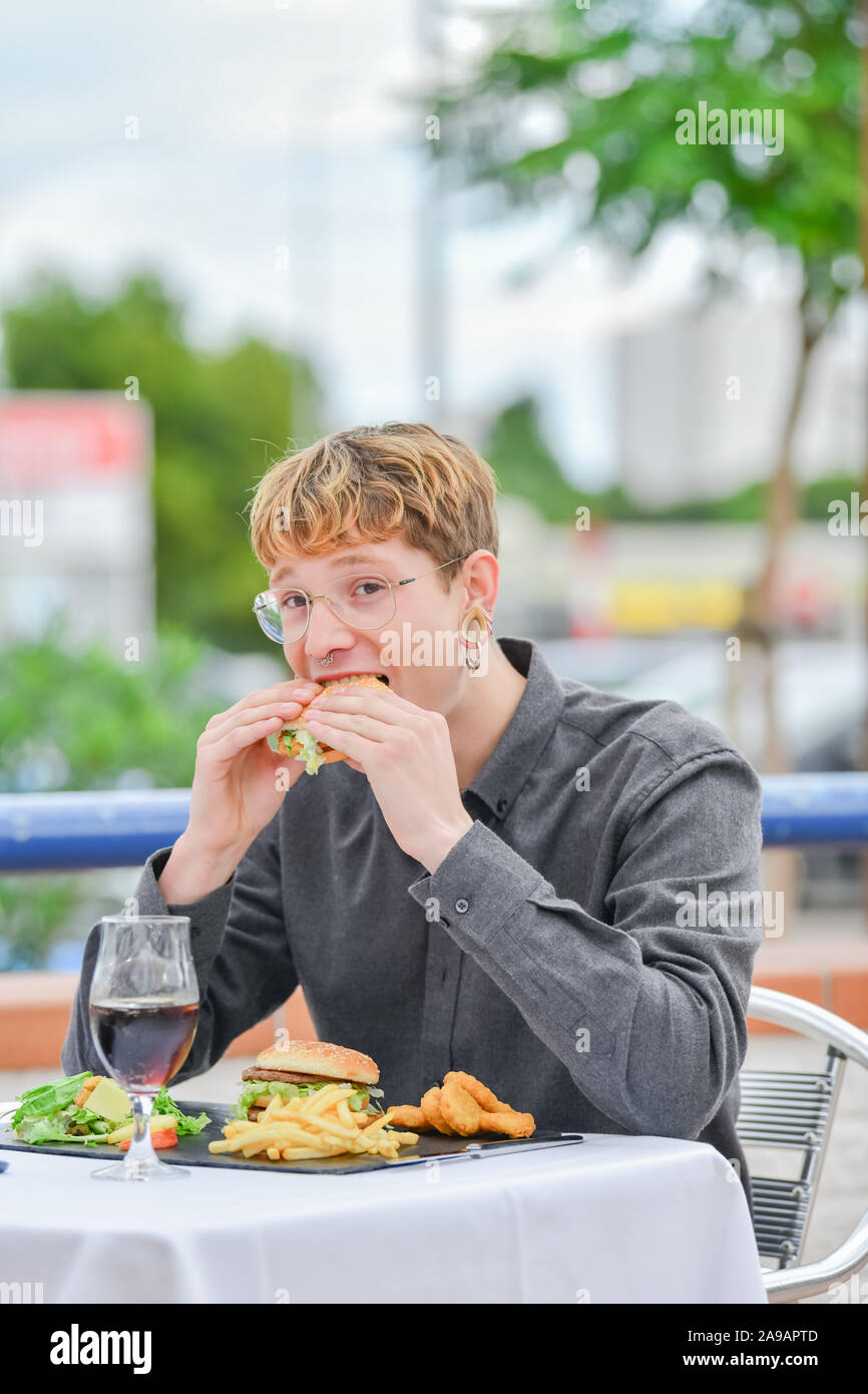 Young man eating burger in street restaurant Stock Photo - Alamy
