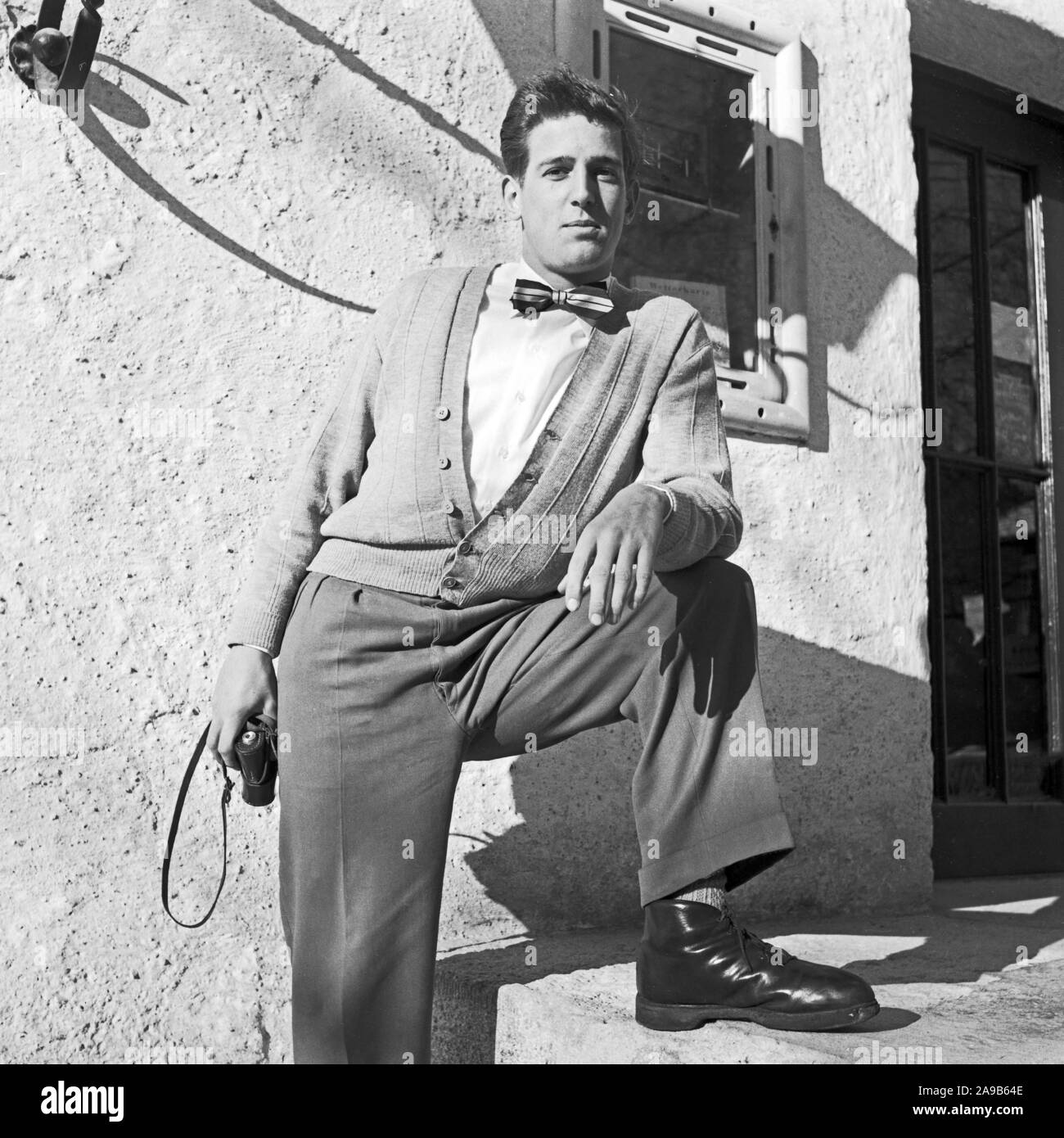 A young man posing with a camera in front of a house, Germany 1957 ...