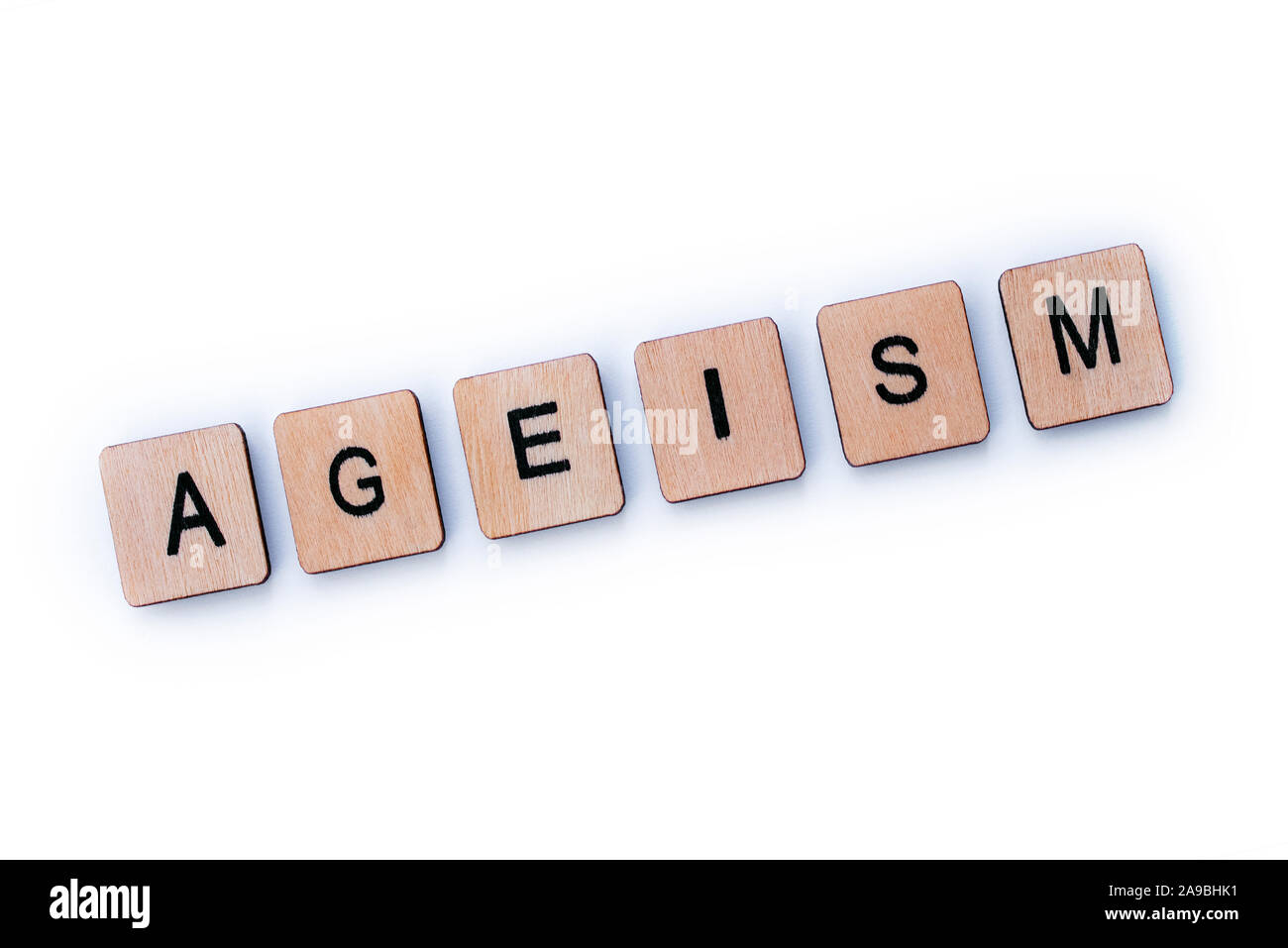 The word AGEISM, spelt with wooden letter tiles over a white background ...