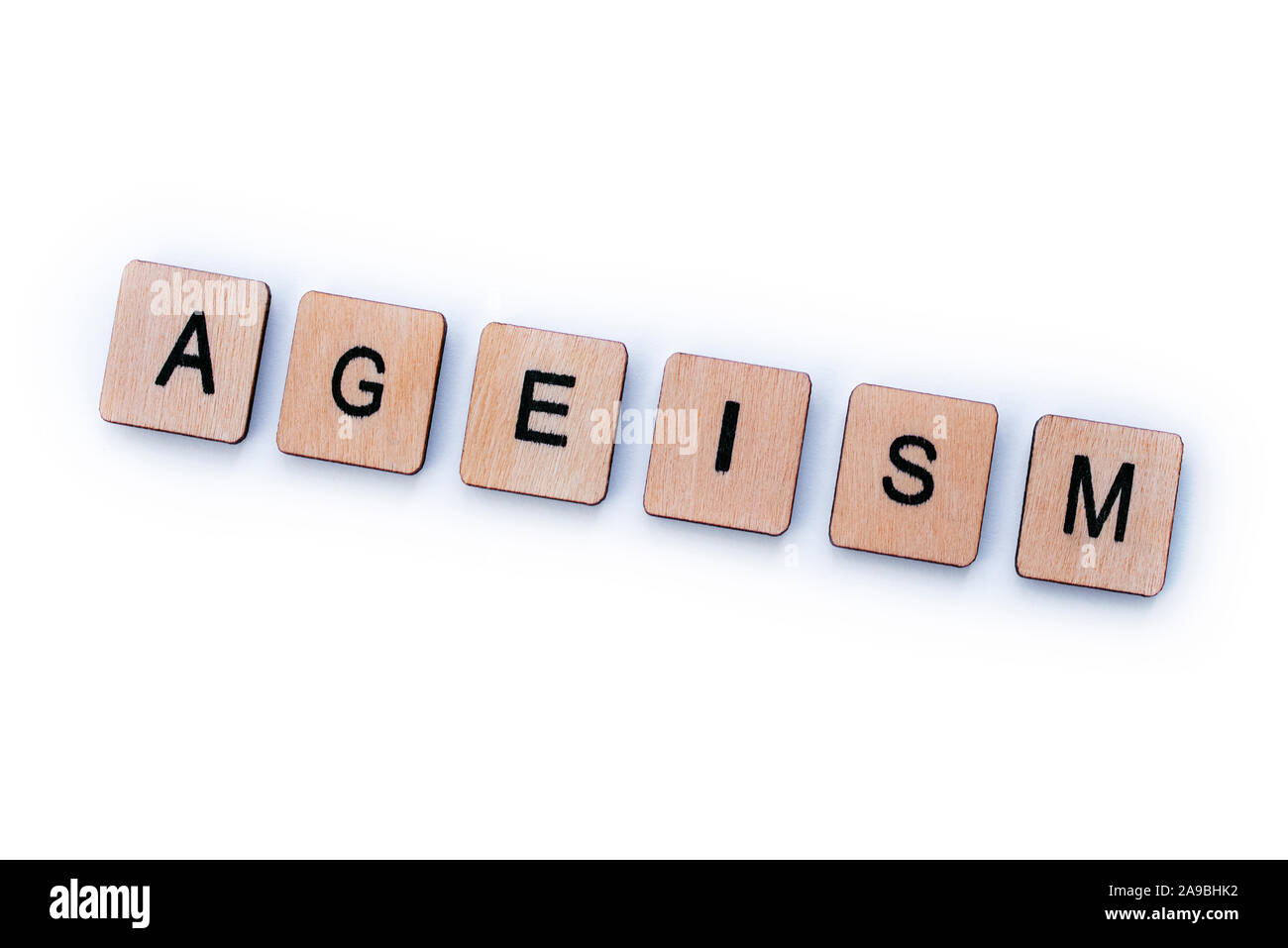 The word AGEISM, spelt with wooden letter tiles over a white background ...