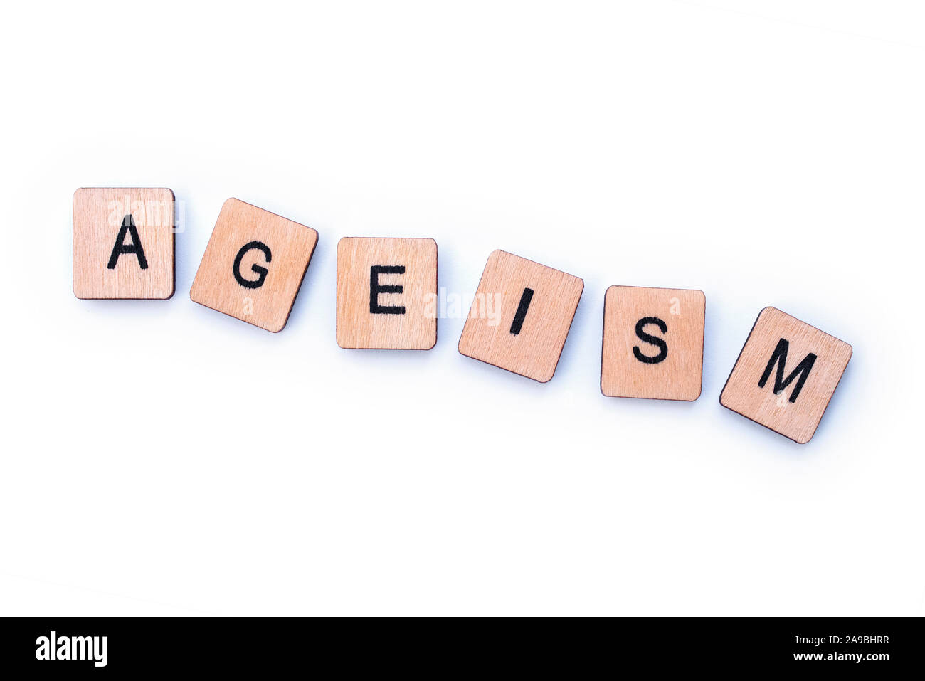 The word AGEISM, spelt with wooden letter tiles over a white background ...