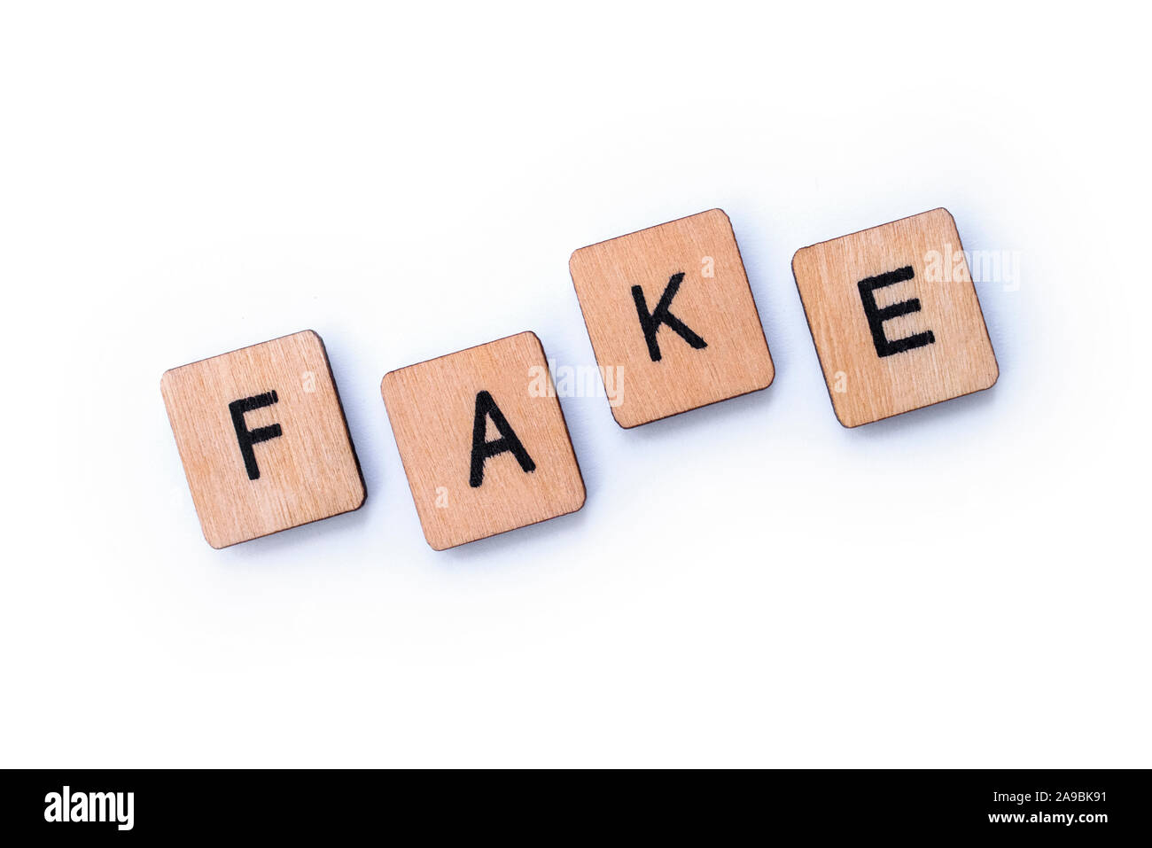 The word FAKE, spelt with wooden letter tiles, over a white background ...