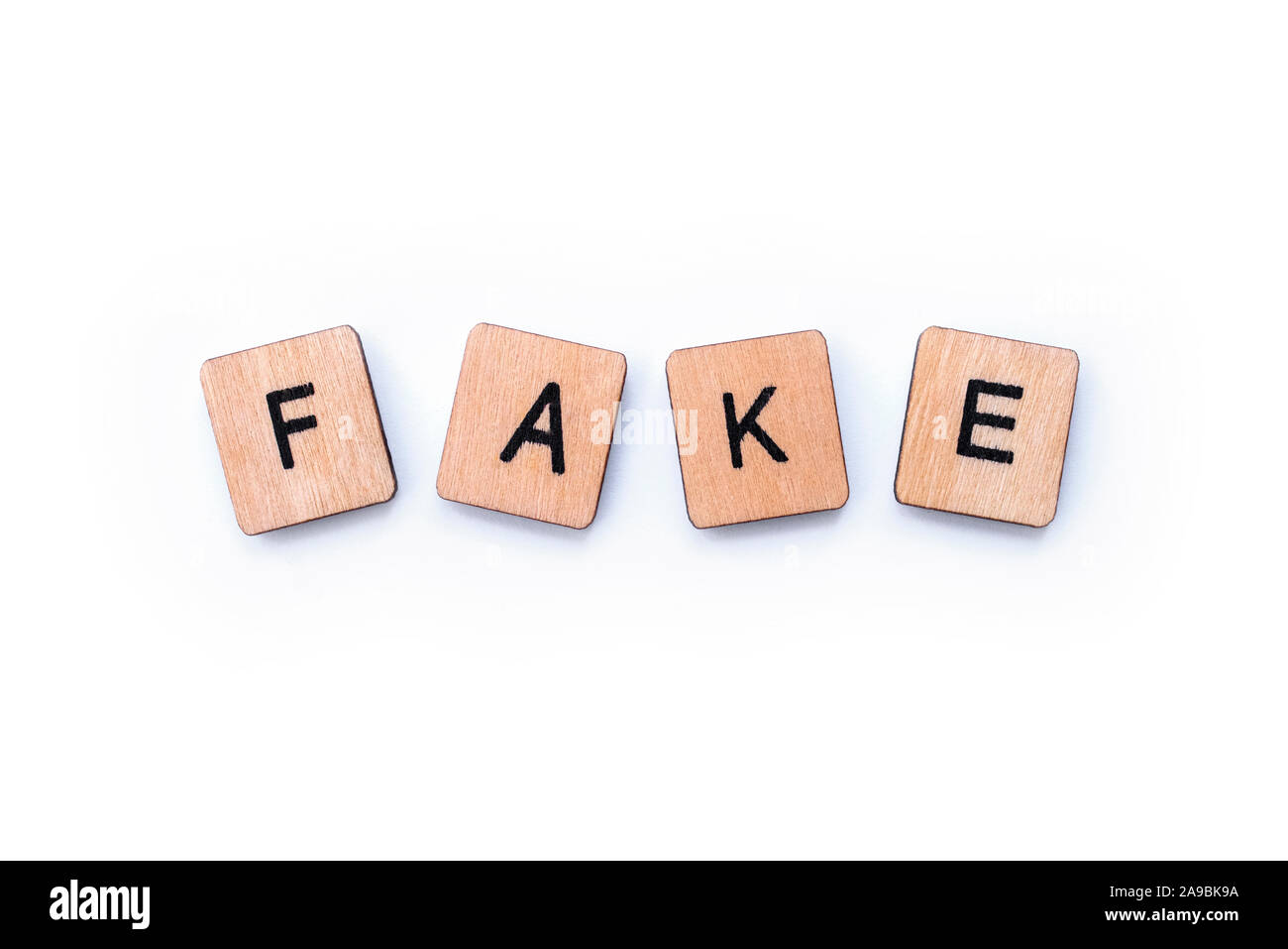 The word FAKE, spelt with wooden letter tiles, over a white background ...