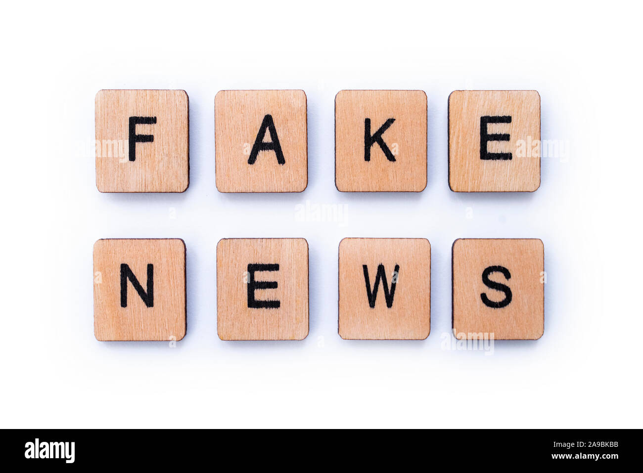 The phrase FAKE NEWS, spelt with wooden letter tiles, over a white ...