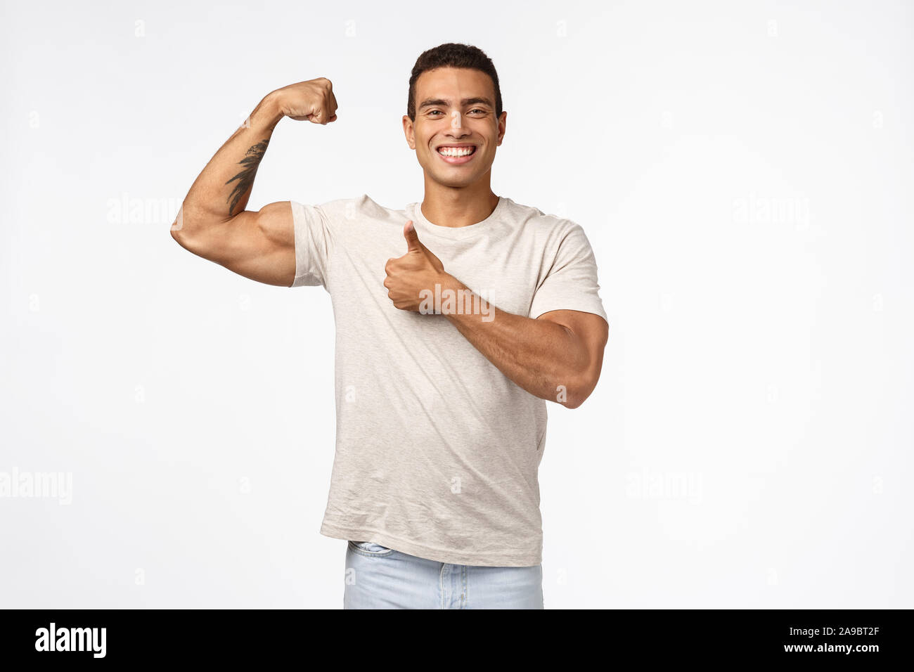 Handsome strong athletic sportsman in casual t-shirt, raise arm, tense ...