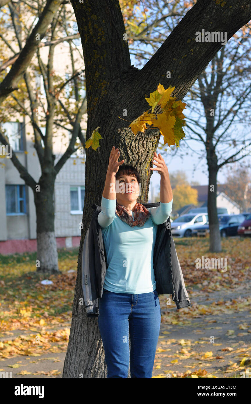 season and people concept - happy young woman throwing maple leaves and ...
