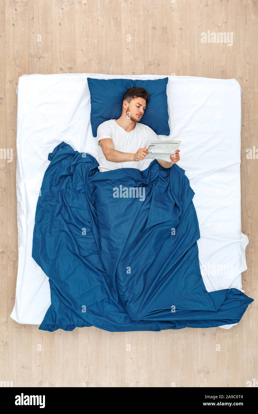 Morning Routine. Guy lying on bed top view reading newpaper ...