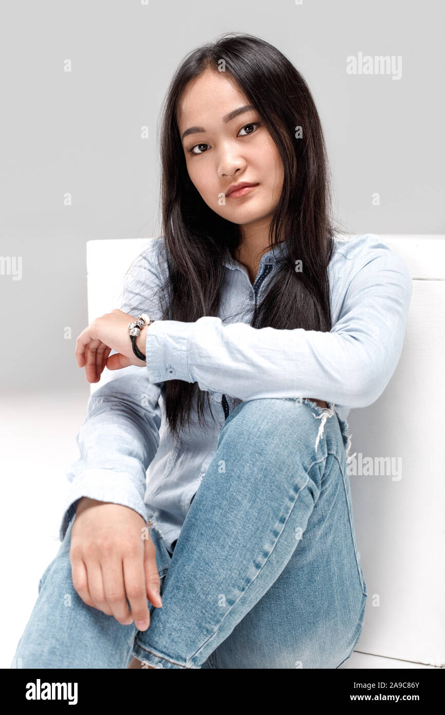 Freestyle. Asian girl sitting leaning on cube isolated on white relaxed ...