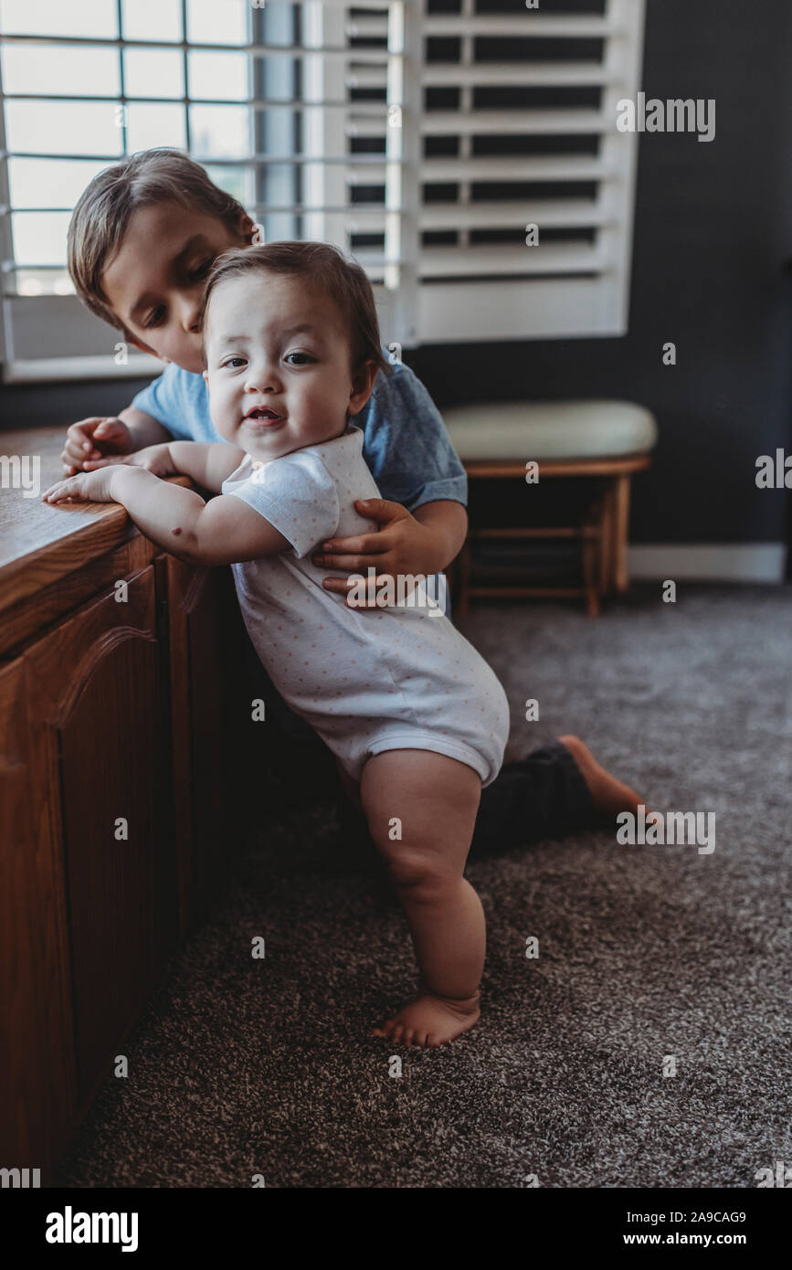 Chubby baby with two teeth standing with help from big brother Stock ...