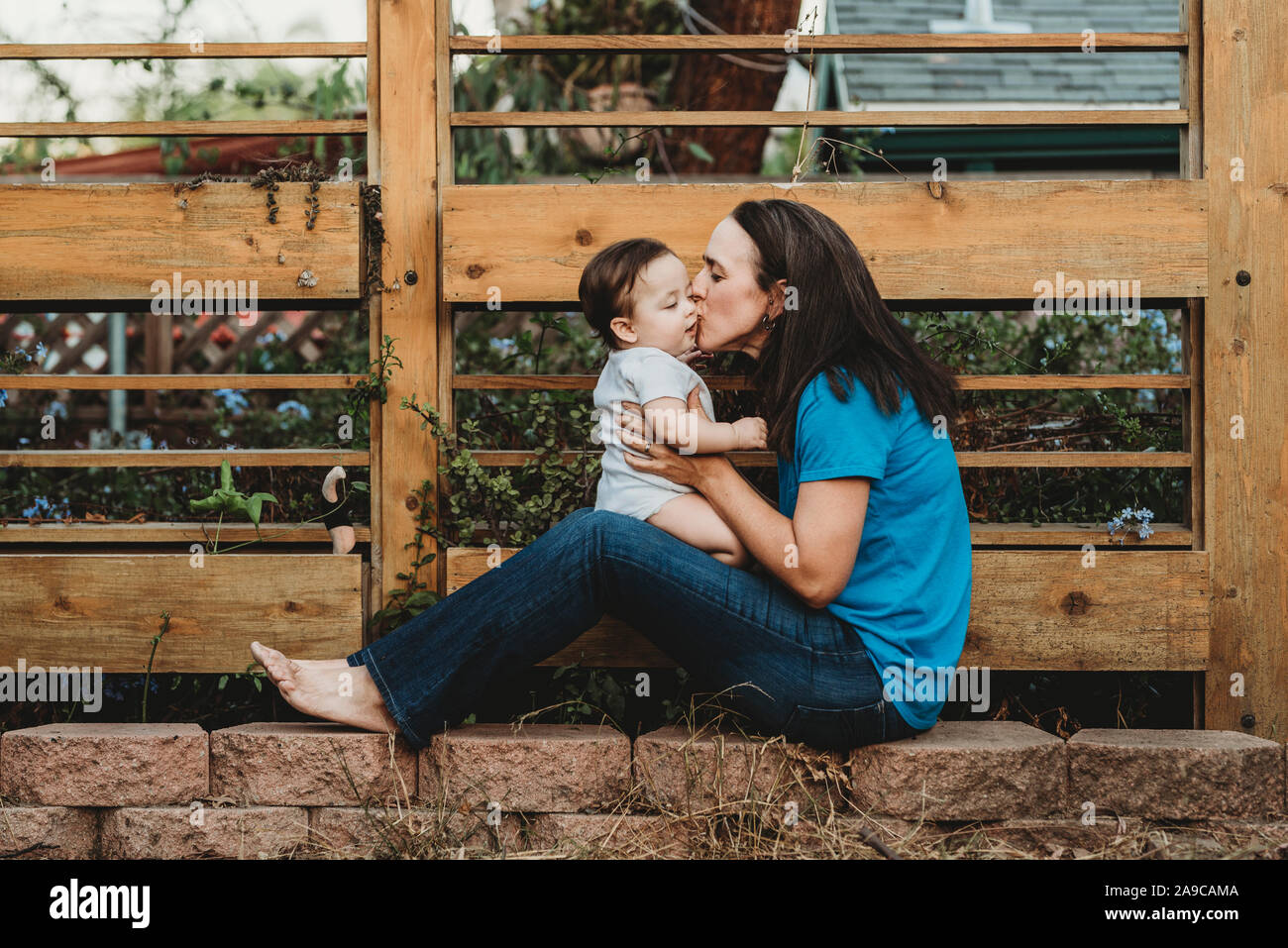 Barefoot mom kissing baby girl while sitting on landscape rocks Stock ...