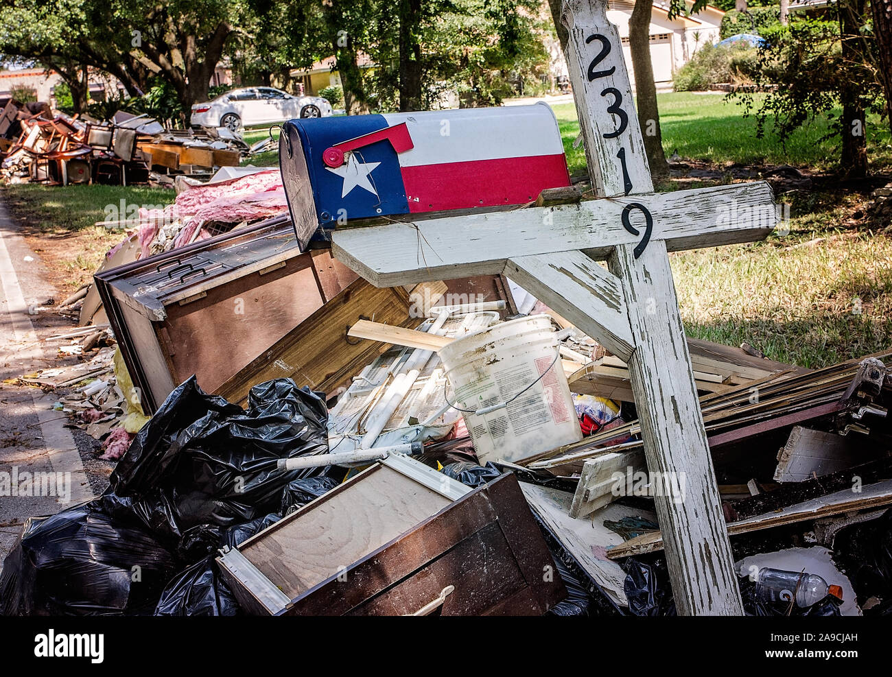 A mailbox featuring a Texas flag motif tilts over a pile of flood ...