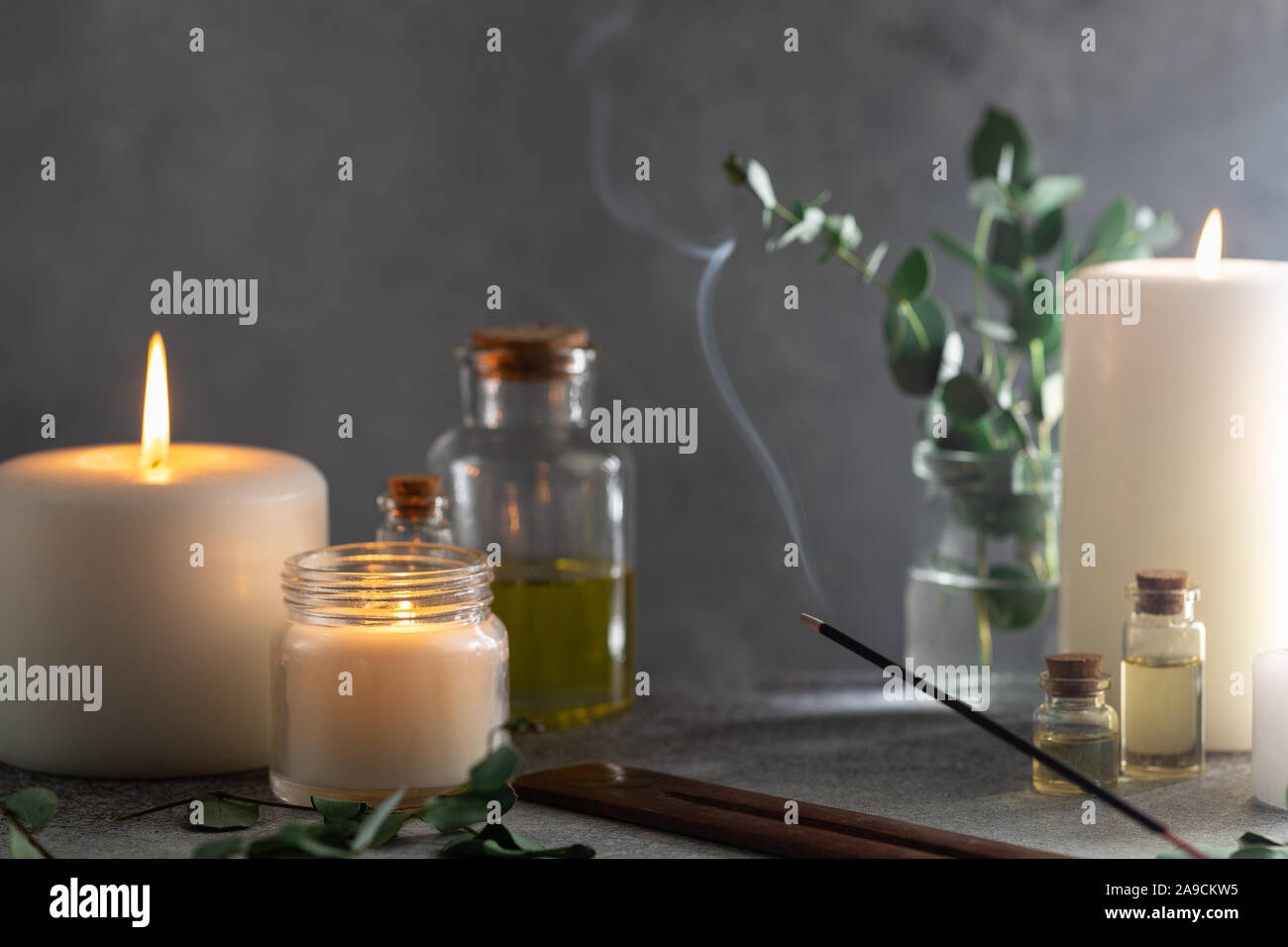 Incense stick with smoke on stone with white candles and essential oils ...