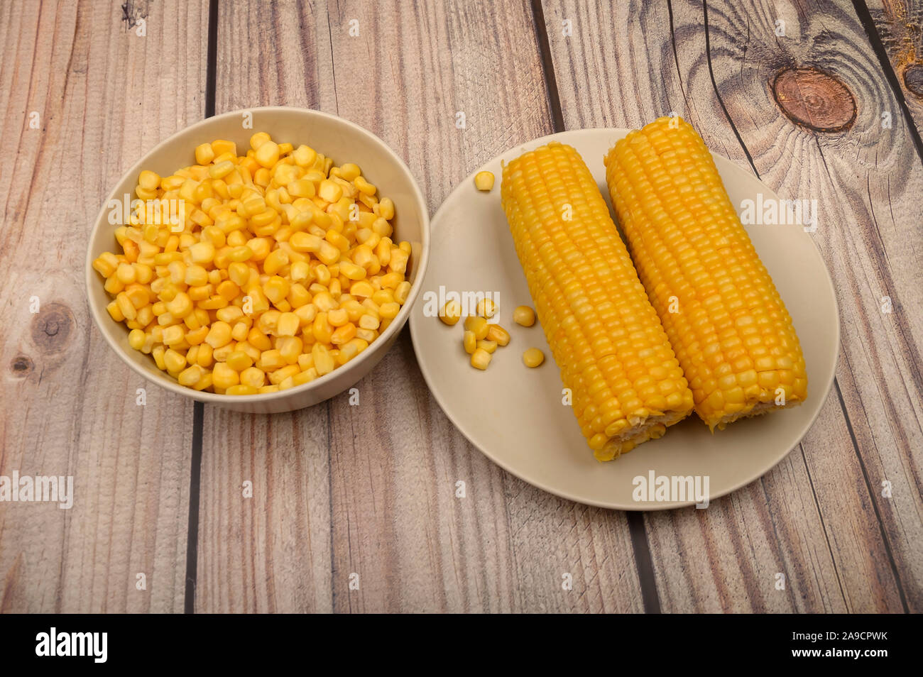 Two ears of boiled corn in a plate and a grain of corn on the table ...