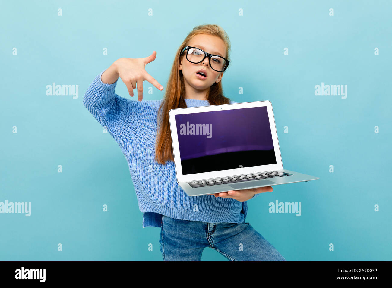 portrait of a dancing girl with a laptop on a background of blue wall ...