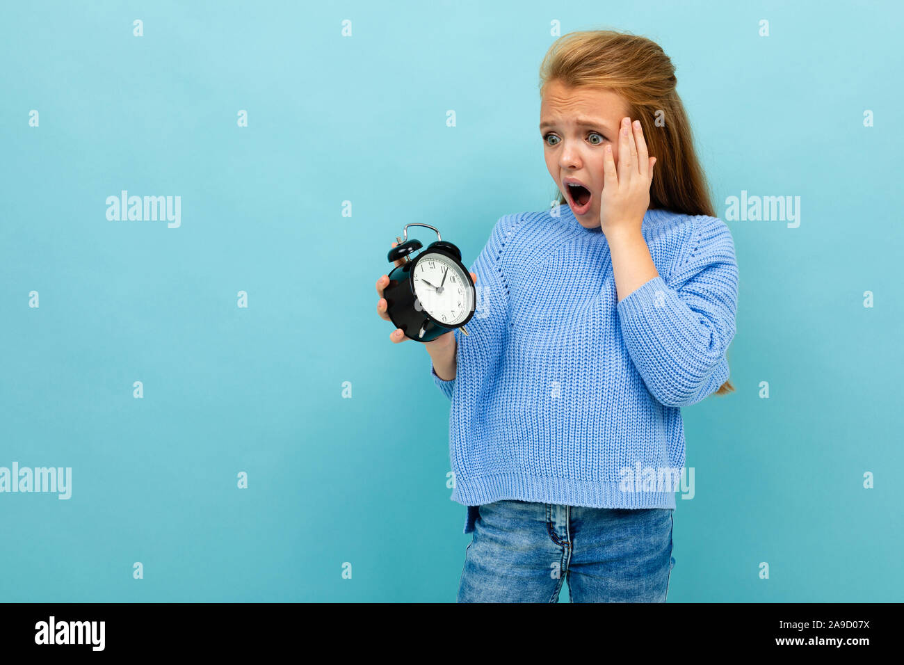 upset beautiful cute girl on a blue background with an alarm clock in ...
