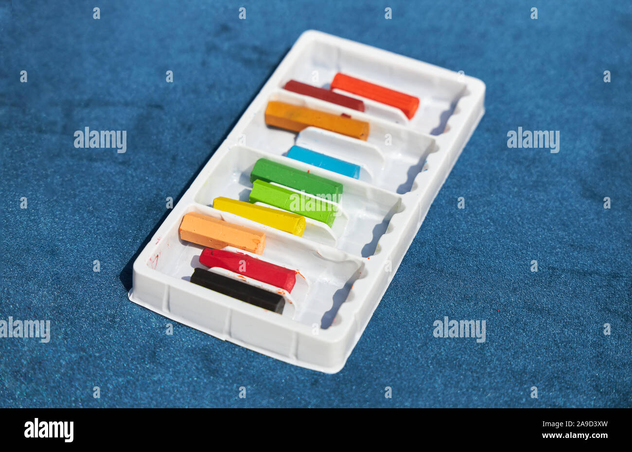 Set of colored crayons in a white box lies on a blue surface Stock ...