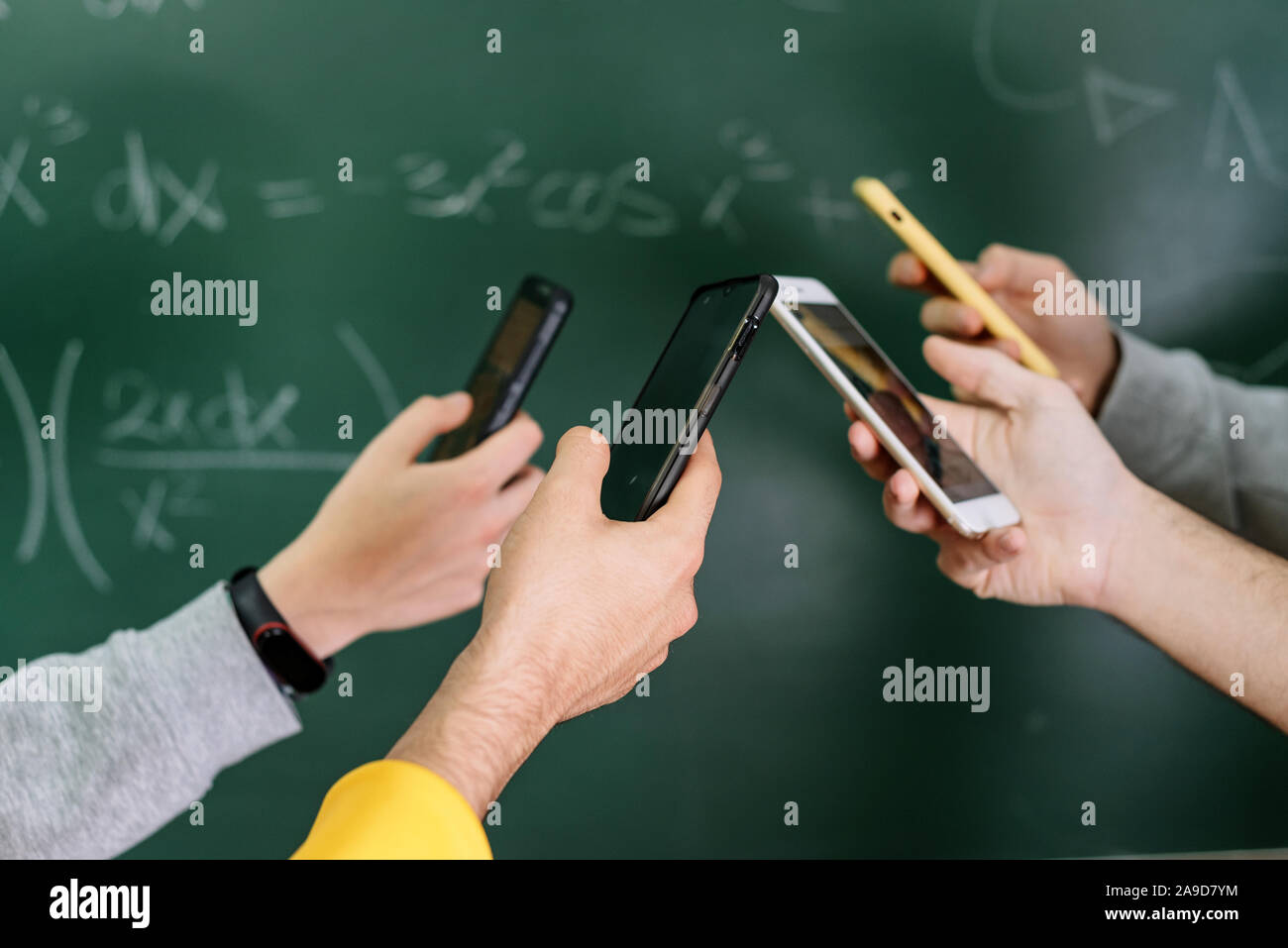 Students using mobile phones in classroom with a chalkboard in the ...