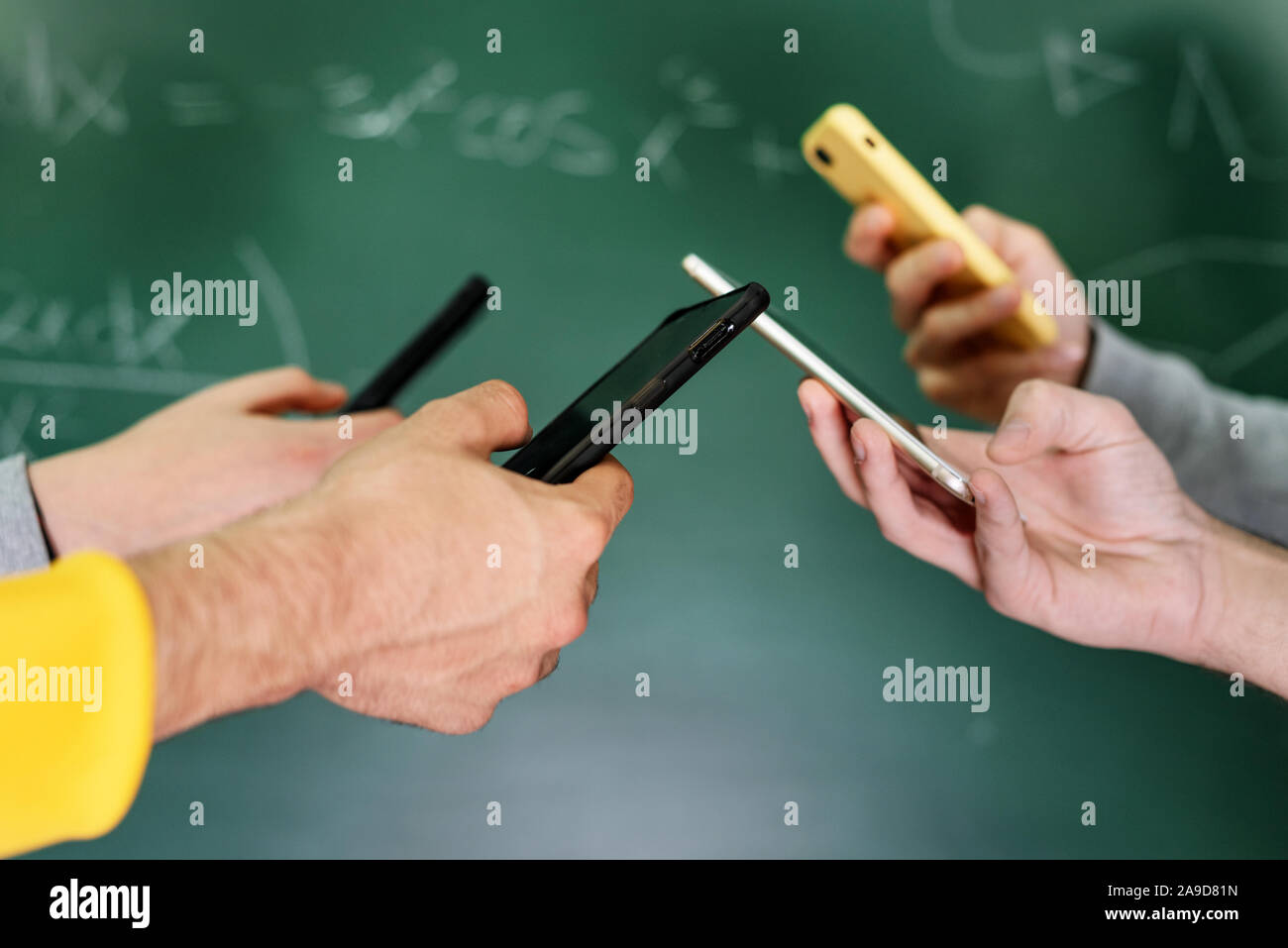 Students using mobile phones in classroom with a chalkboard in the ...