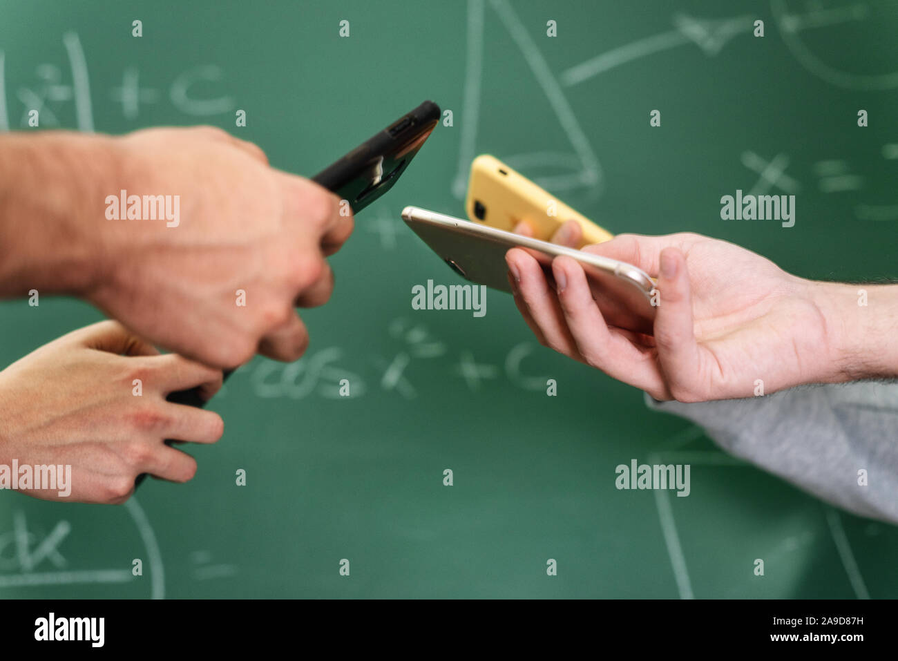 Students using mobile phones in classroom with a chalkboard in the ...