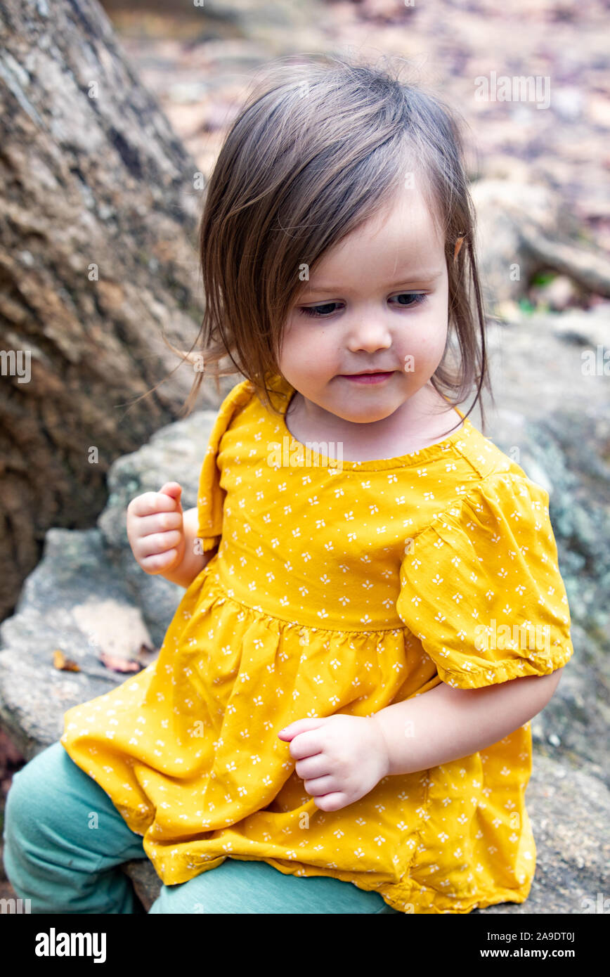 Toddler sitting on a rock looking at something in nature Stock Photo ...