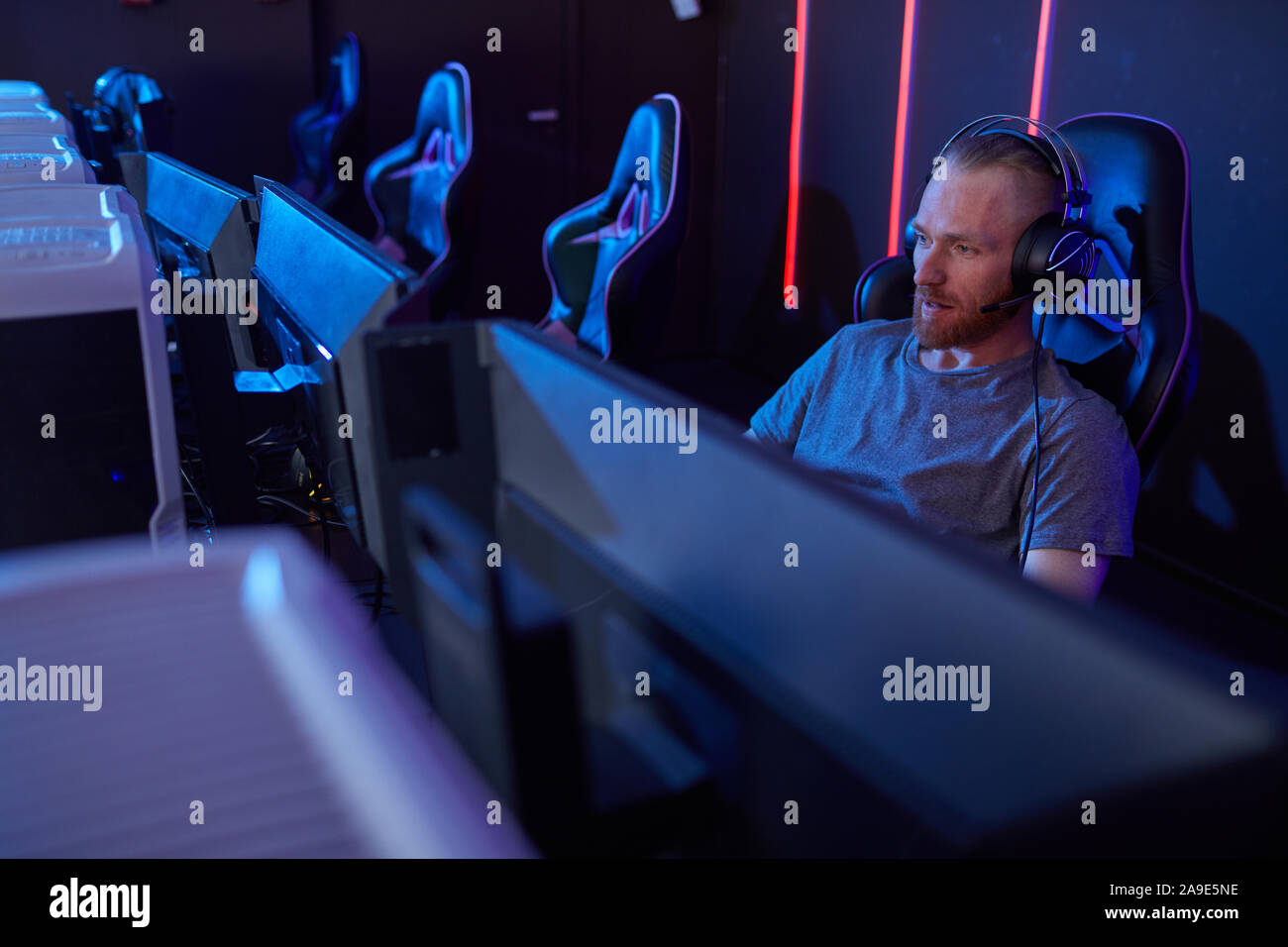 Young bearded man wearing headphones sitting in front of computers in ...