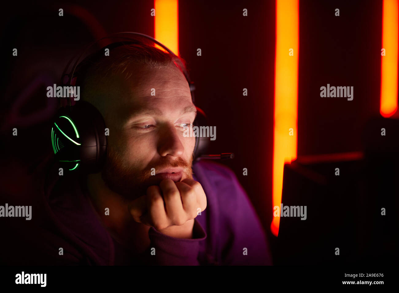 Young bearded man wearing gaming headphones with backlight looking at ...