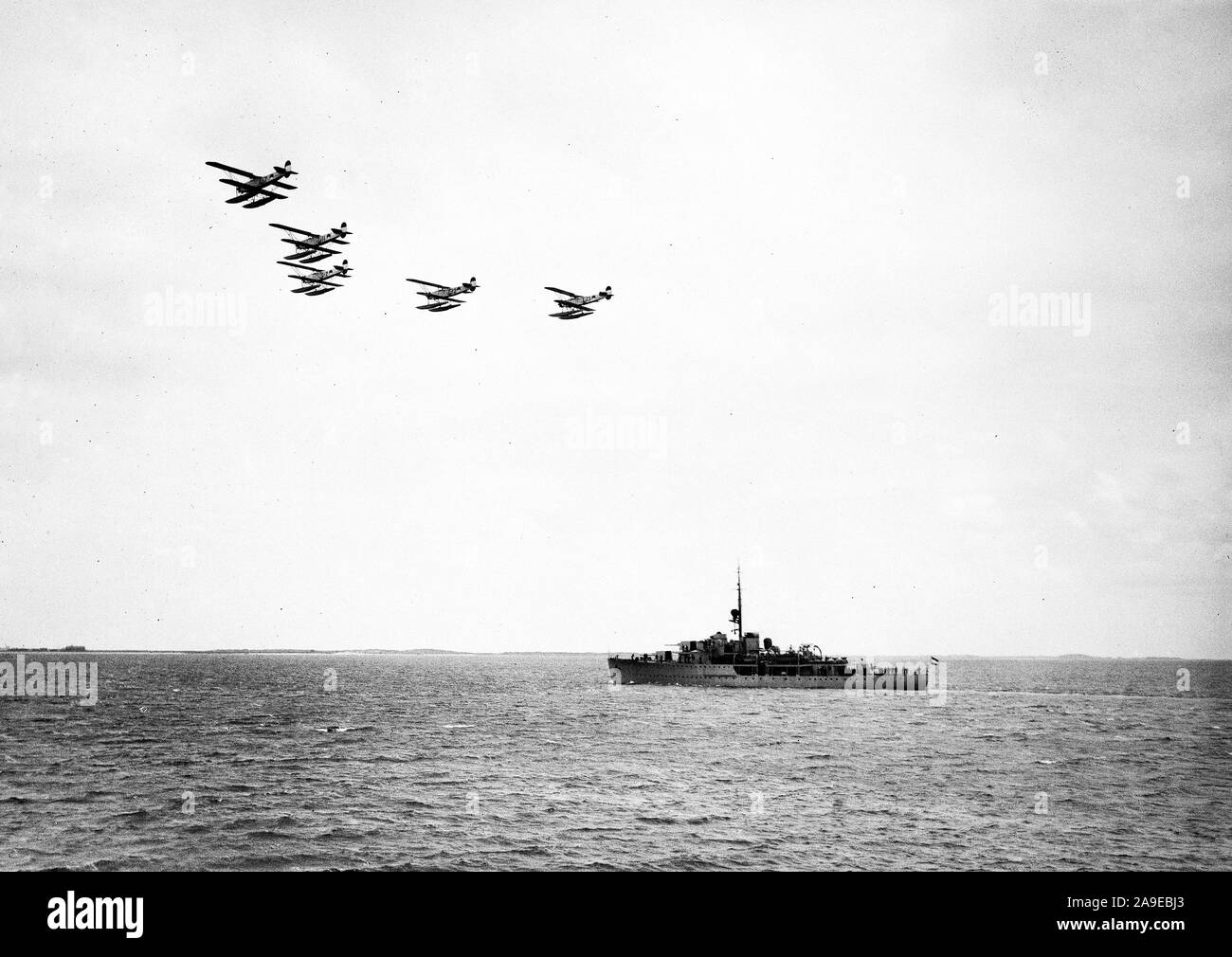 Five seaplanes fly above a naval ship in formation, presumably at the ...