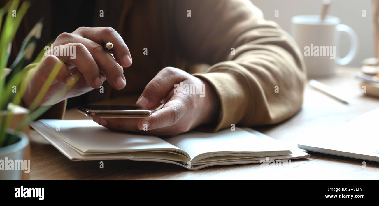 Cropped shot of young man working on his project while using smartphone ...
