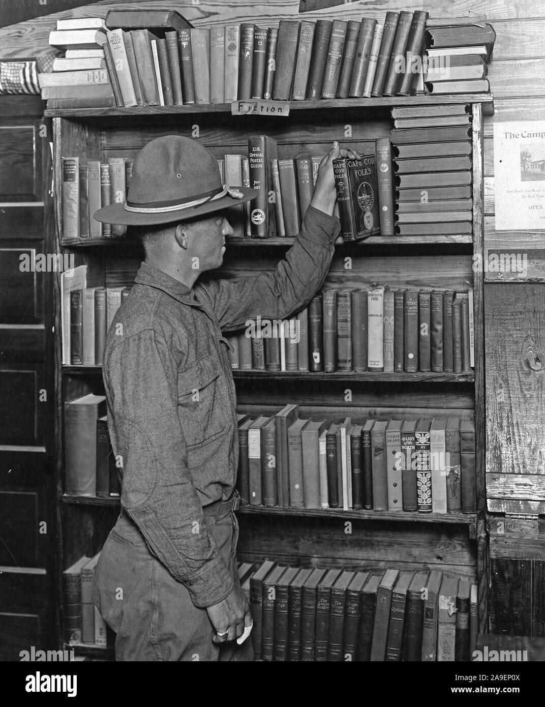 World War I era soldier looking at books on a shelf in a camp library ...