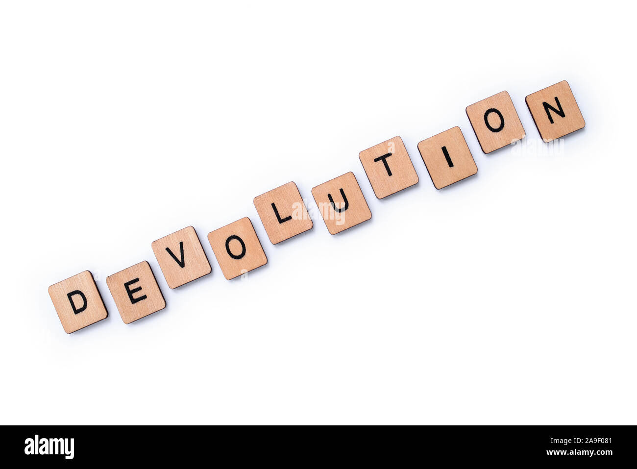 The word DEVOLUTION, spelt with wooden letter tiles over a plain white ...