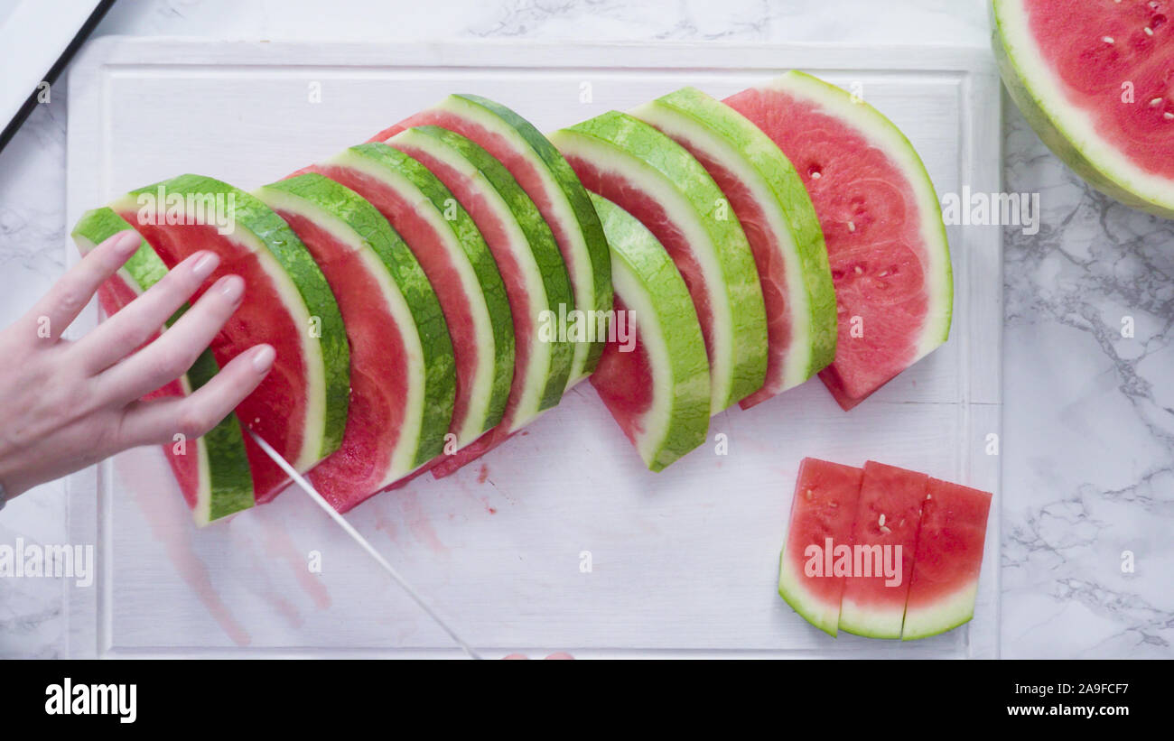 Flat lay. Slicing red watermelon into small pieces on a white cutting ...