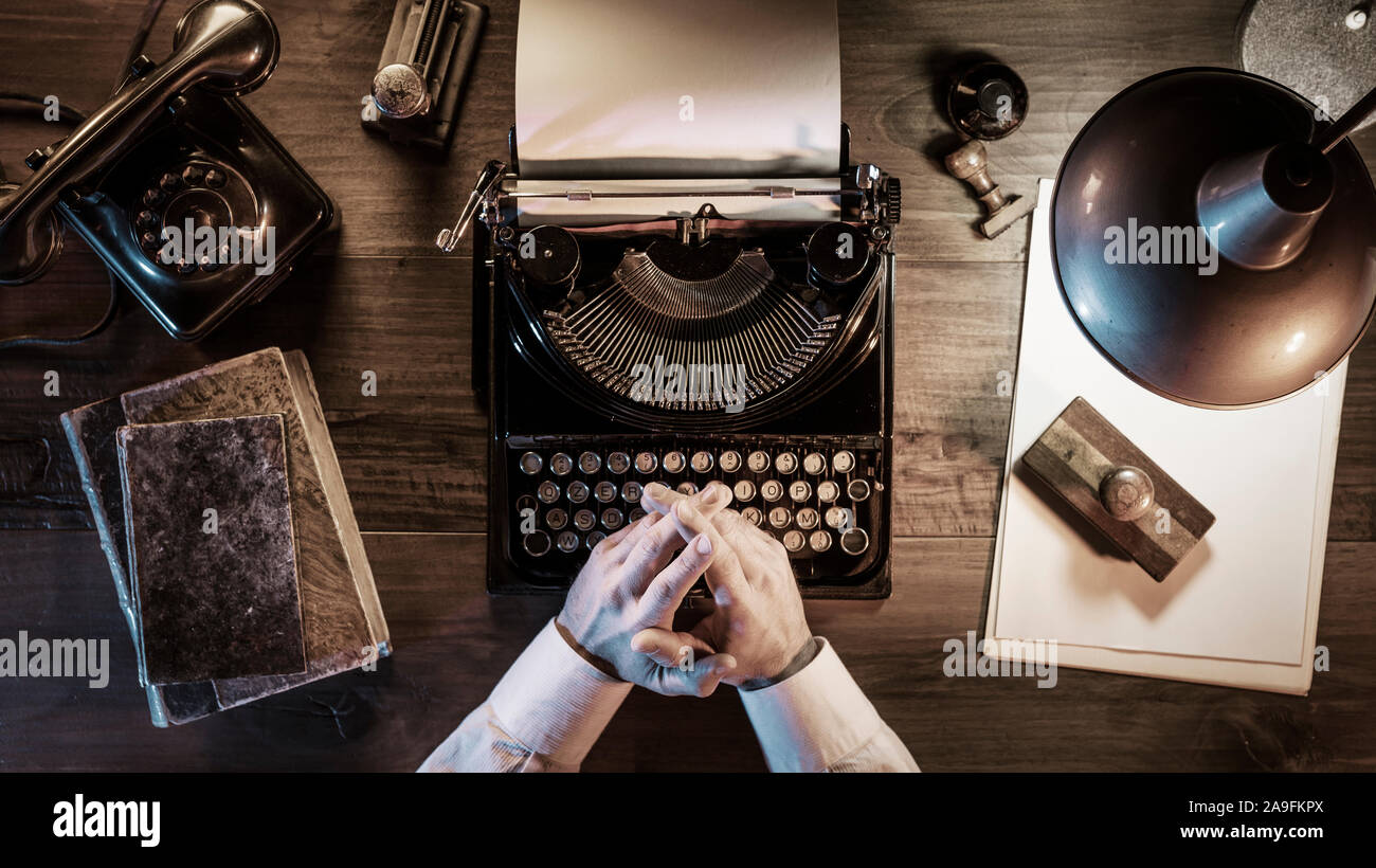 1950s style journalist working in his office at night, he is typing ...