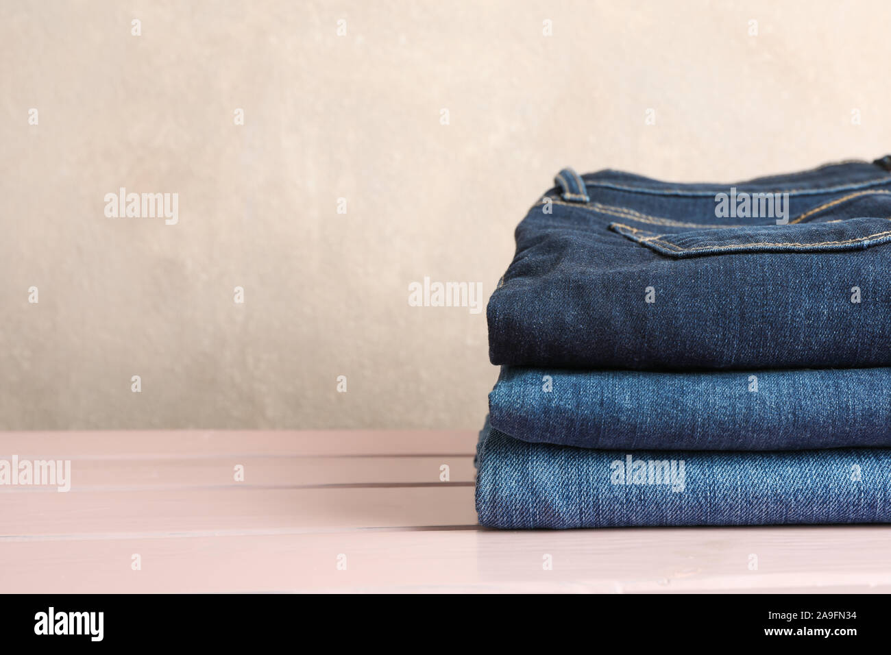 Stack of jeans pants on light pink background, space for text Stock ...