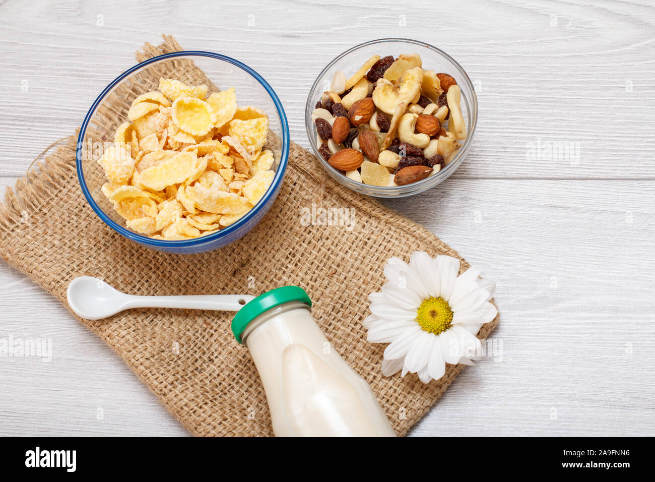 Glass bottle of fresh milk, bowls with muesli and cornflakes, chamomile ...