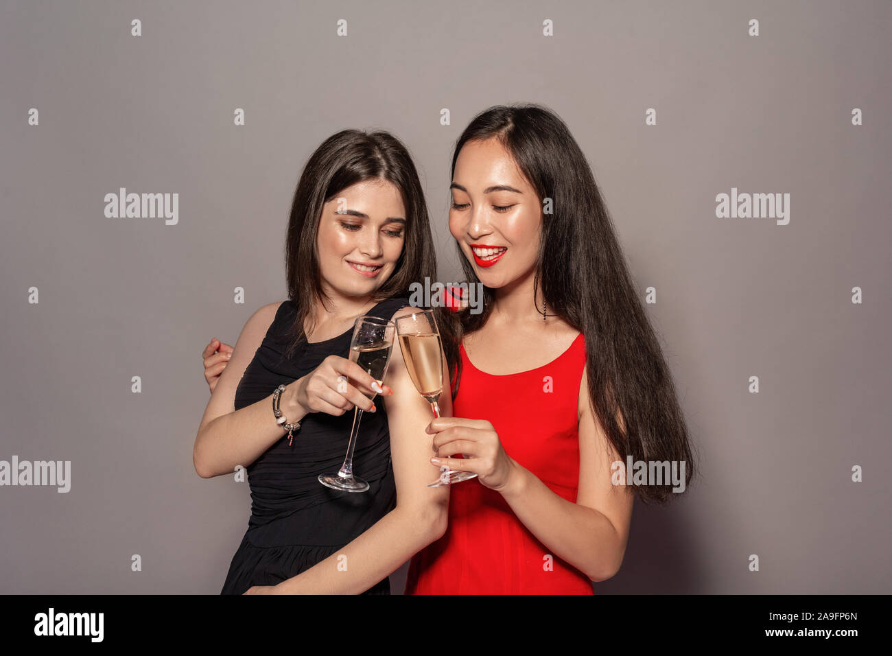 Freestyle. Young girls in dresses standing hugging isolated on gray ...