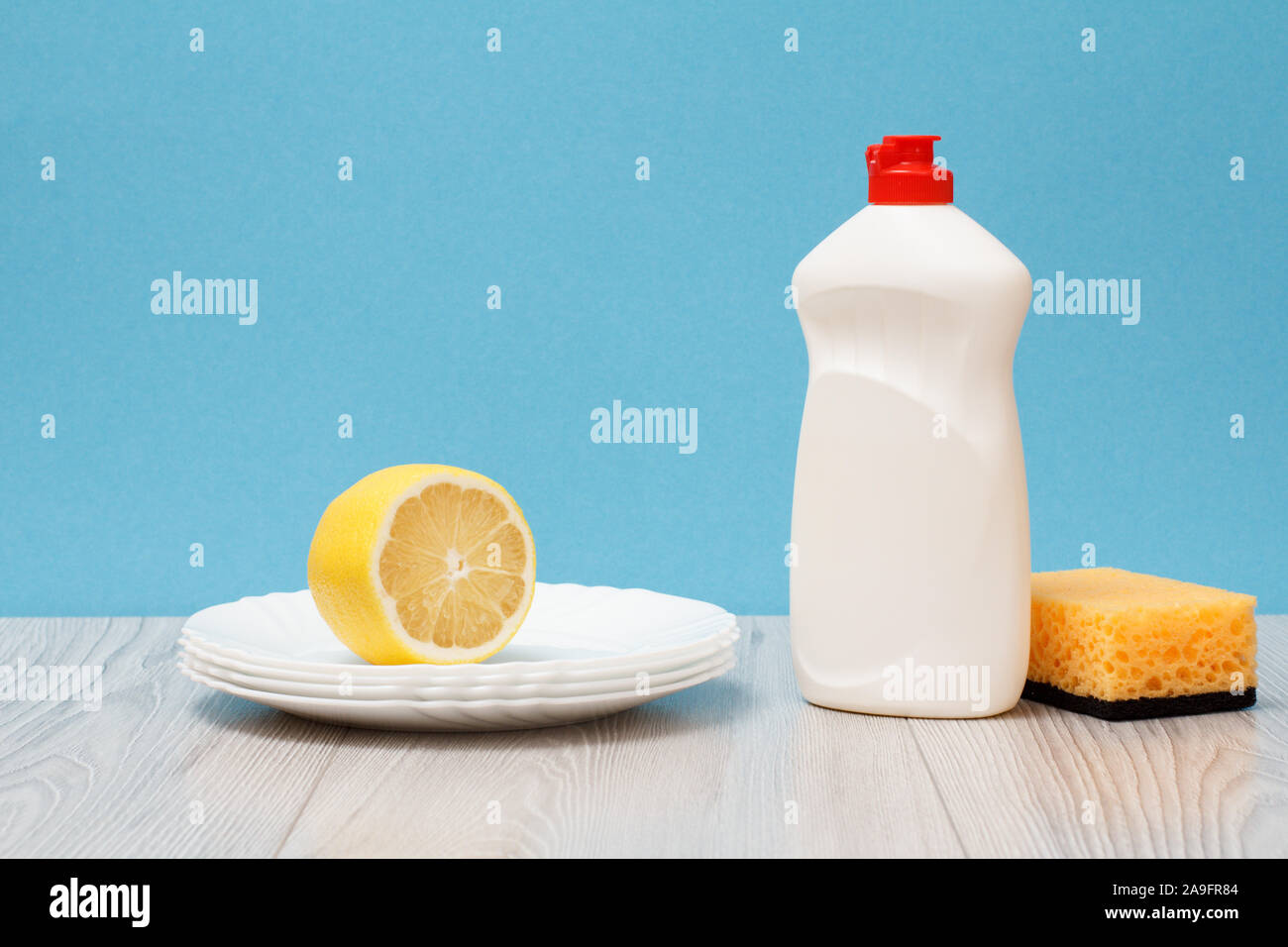 Plastic bottle of dishwashing liquid, clean plates, lemon and sponge on ...