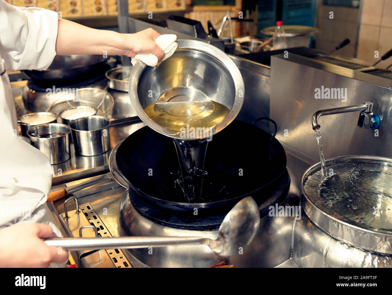 Chef is pouring cooking oil in wok, toned Stock Photo - Alamy