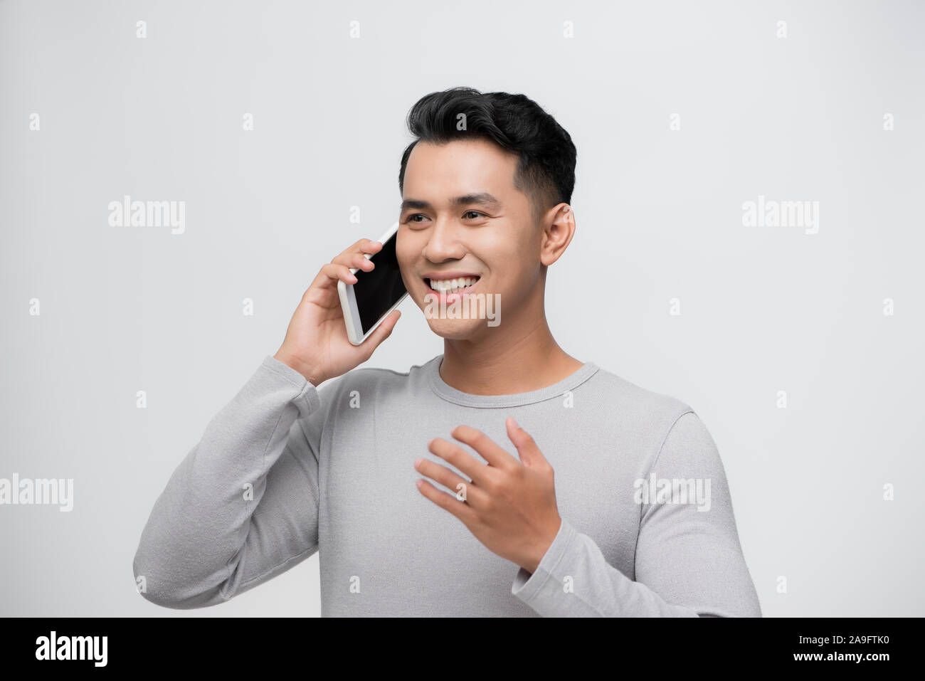 Thoughtful happy asian man smiling while talking on mobile phone ...