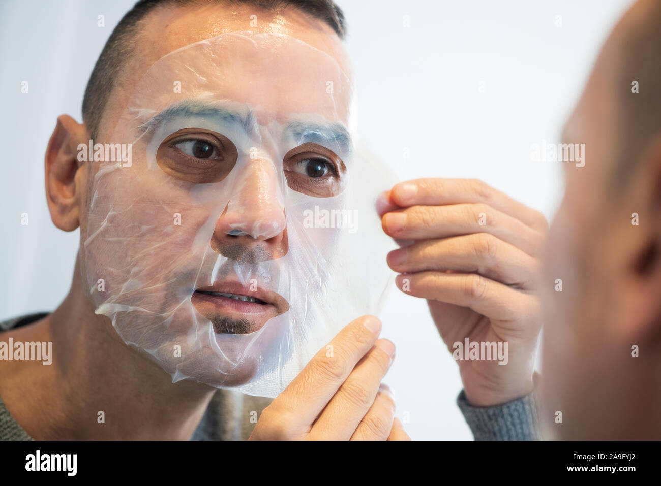 closeup of a handsome caucasian man applying a bio-cellulose sheet mask ...