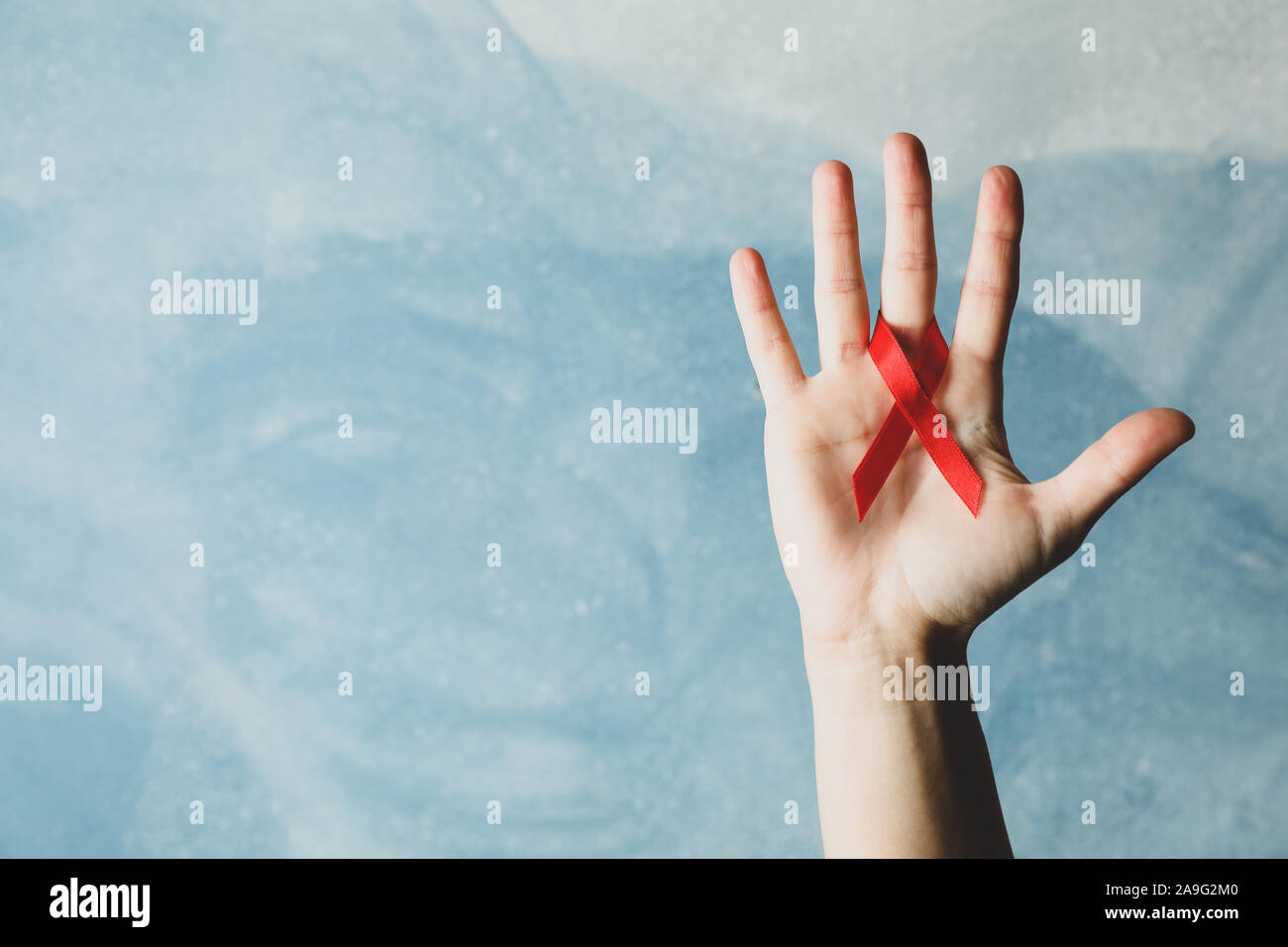 Hand and red awareness ribbon against blue background, space for text ...