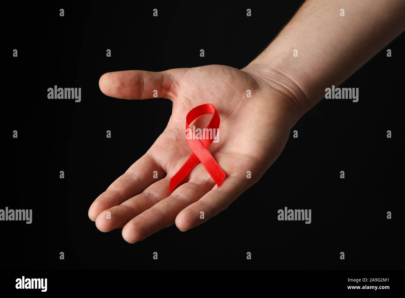 Hand and red awareness ribbon against black background, space for text ...