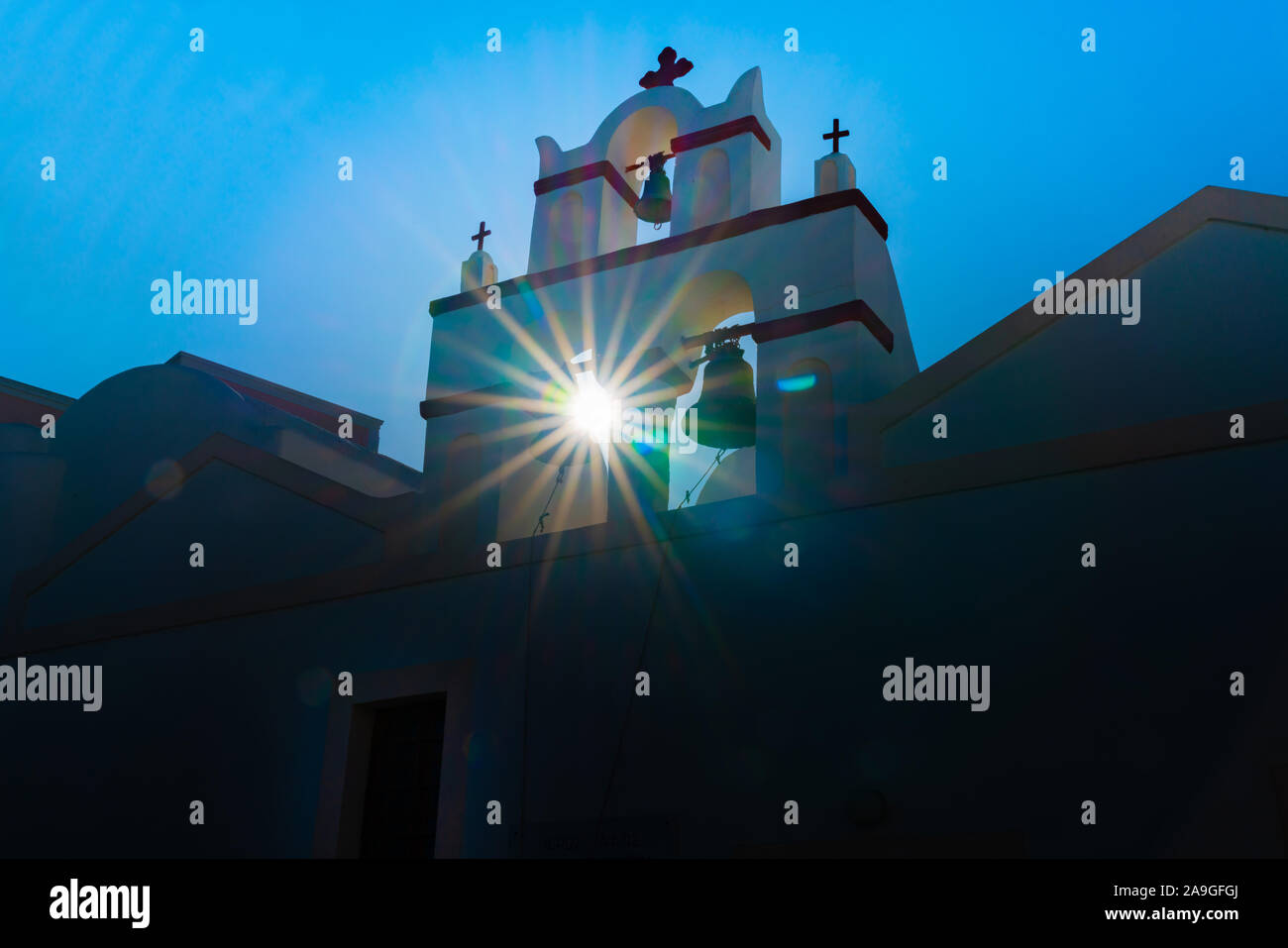Traditional Greek church bell tower back-lit by sun with starburst and ...
