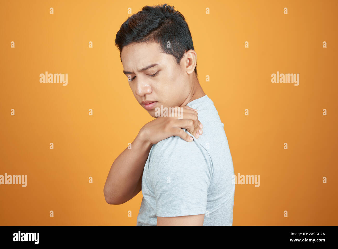 Young Asian man in casual with shoulder pain. Isolated on orange ...
