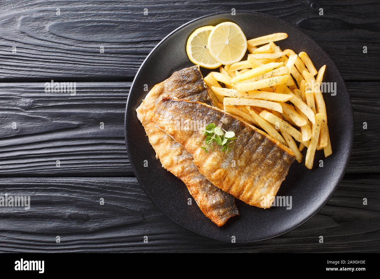 Spicy grilled sea bass fillet with crispy skin with french fries close ...