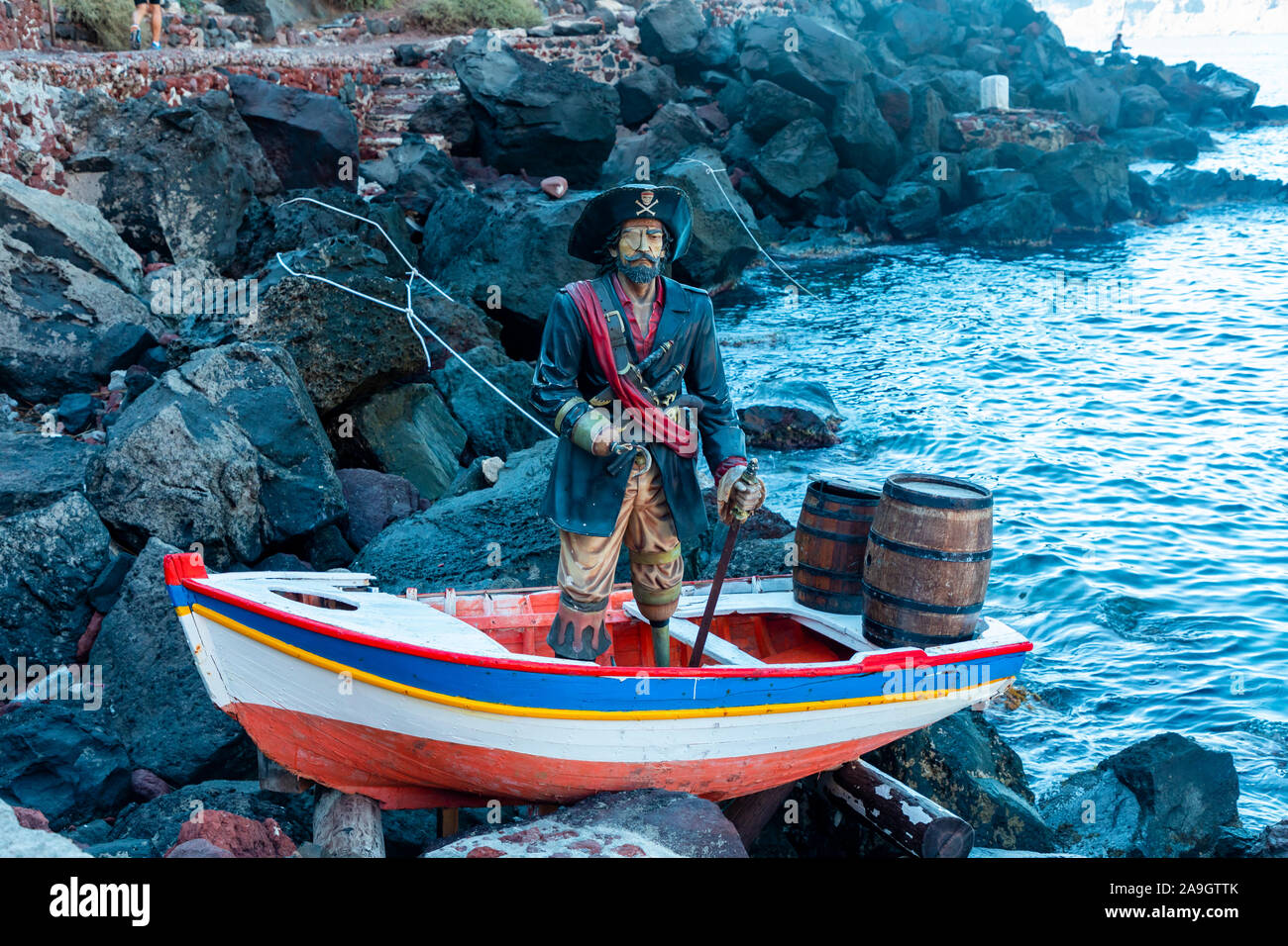A pirate statue in a small boat near black rocks in the Greek Islands ...