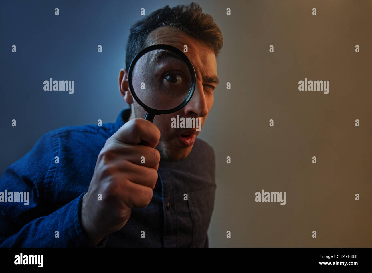Shocked man with magnifying glass on grey background. Curious young man ...