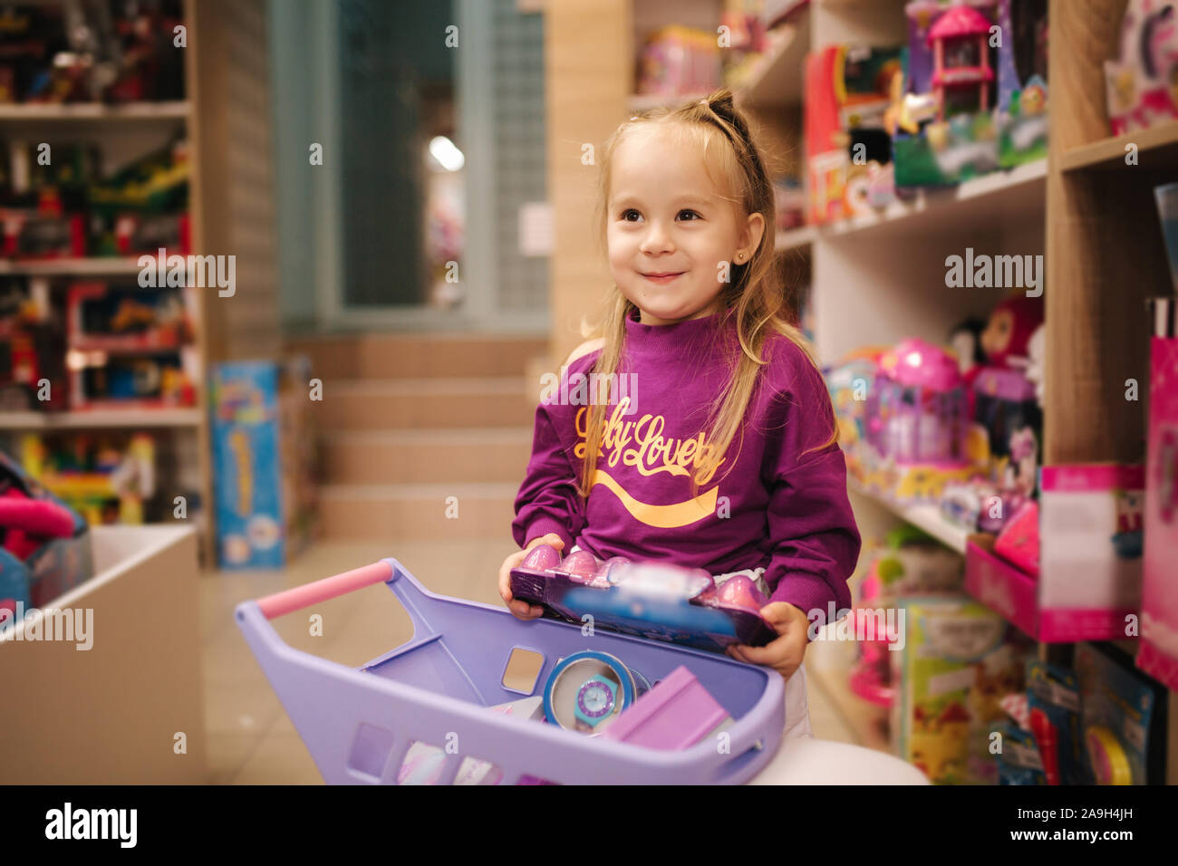 Little girl with small shopping cart in kids mall. Happy girl choosing ...
