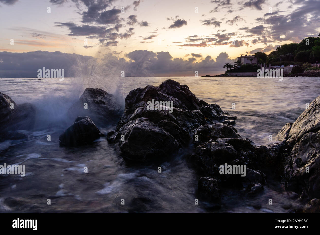 Wave hitting the rocky shoreline at sunrise Stock Photo - Alamy