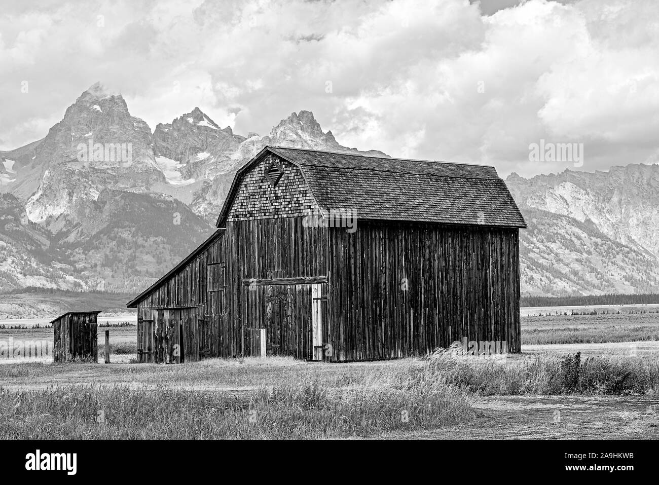 Old Mormon barn with fields and mountains beyond. Black and white image ...