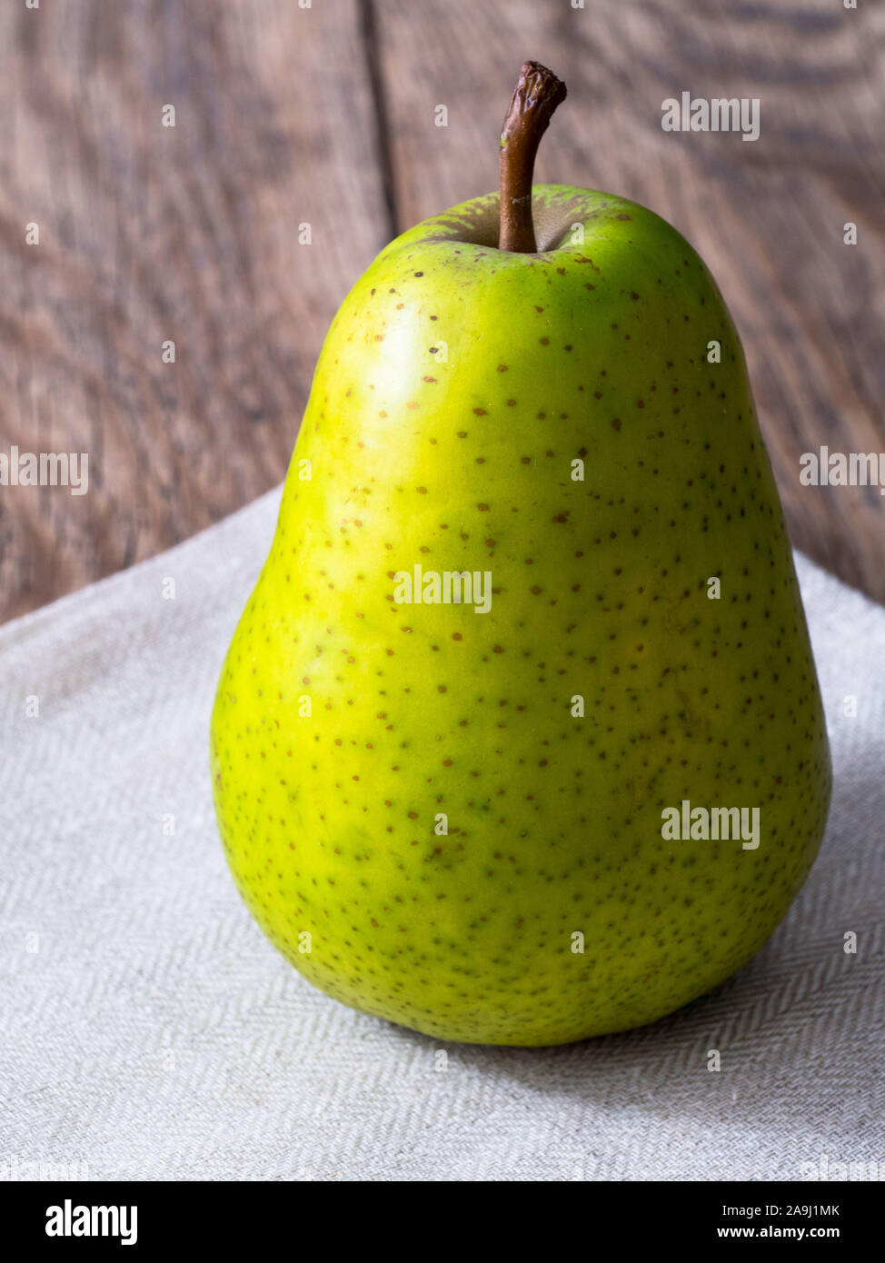 large green pear, one stands on a linen cloth, on a wooden table. Image ...